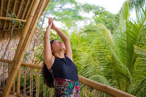 웰빙과 건강한 라이프 스타일에서 열대 정글 보기와 아름다운 나무 조글로 스튜디오에서 야외에서 요가와 명상 운동을 연습하는 젊은 자연적이고 매력적인 아시아 여성 명상하기에