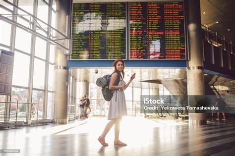 테마 여행 과 트라노 스포츠 빨간 전화를 들고 일정을 보고 기차역 이나 터미널 안에 서 드레스와 배낭에 아름 다운 젊은 백인 여자 통신 기술을 사용 하 여 도착에 대한 스톡