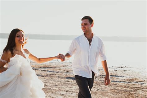 웨딩 커플은 바다 해변에서 달리고 있습니다 화창한 여름 사진 기차가 있는 오프 숄더 드레스를 입고 머리를 숙인 신부 바다의