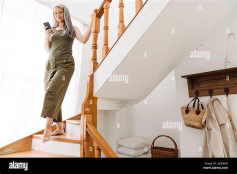 Mature Asian Woman Using Cellphone While Going Down Stairs At Home