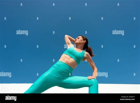 Mid Adult Woman Doing A Side Angle Body Stretch Outside With Blue Sky Background Stock Photo
