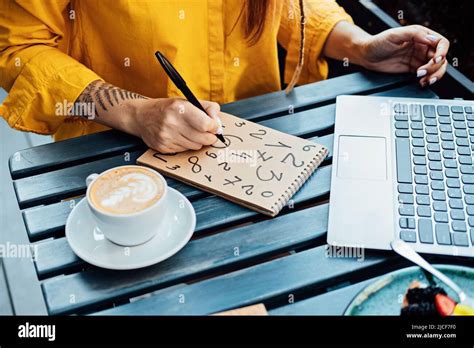 Woman Freelancer Writing Numbers In Notepad While Working With Laptop