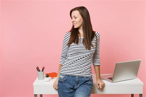 젊은 여자 옆으로 일을 찾고 하 고 파스텔 핑크 배경에 고립 된 Pc 노트북과 흰색 책상에 기대어 캐주얼 옷에 꽤 성과 비즈니스 경력 개념입니다 광고에 대 한 공간을 복사