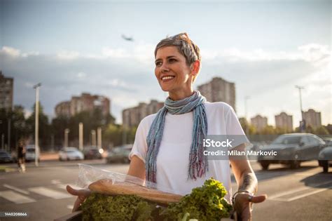 성숙한 여성이 슈퍼마켓 밖 주차장에 서서 여객기가 그녀의 뒤를 날아갈 때 구입 한 음식과 야채 상자를 들고 서 있습니다 45 49세에 대한 스톡 사진 및 기타 이미지