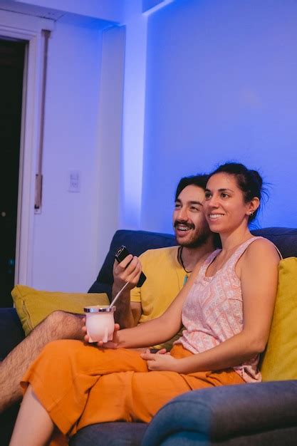 Joven pareja latina sentada en un sofá bebiendo mate mientras usa su control remoto de tv foto