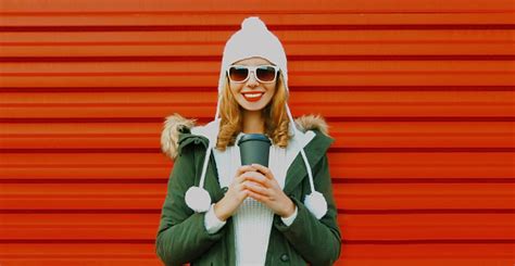 빨간 배경에 폼 폼이 달린 흰색 모자를 쓰고 커피 컵을 들고 미소짓는 젊은 여성의 겨울 초상화 20 29세에 대한 스톡 사진 및 기타 이미지 Istock