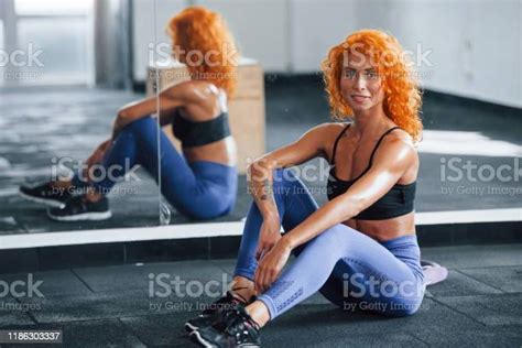 앉아서 휴식을 취하십시오 스포티 한 빨간 머리 소녀는 낮에 체육관에서 피트니스 일을가지고있다 근육질의 체형 가냘픈에 대한 스톡