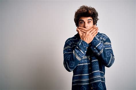 고립 된 흰색 배경 위에 서있는 캐주얼 셔츠를 입은 젊은 잘생긴 남자는 실수로 손으로 입을 덮는 충격을 받았습니다 비밀 개념입니다 가리기에 대한 스톡 사진 및 기타 이미지