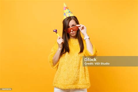생일 모자 오렌지 서 노란색 배경에 고립 축 하 연주와 함께 재미 있는 안경 파이프를 들고 의아해 여자 Bewildered