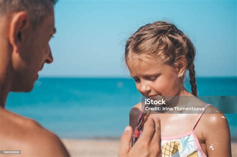 아버지는 해변에서 딸의 등에 보호 크림을 바르고 있습니다 한 남자가 아이의 몸에 자외선 차단제 로션을 들고 있다 바다에 의해 자외선 차단제를 가진 귀여운 어린 소녀 공간을