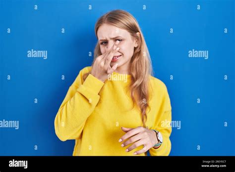 Young Caucasian Woman Standing Over Blue Background Smelling Something