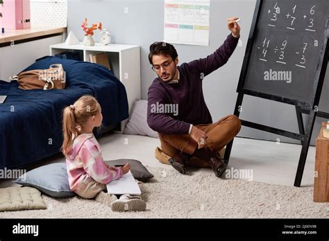 Math Tutor Sitting At Blackboard And Pointing At Example While Explaining Rule To Girl Stock