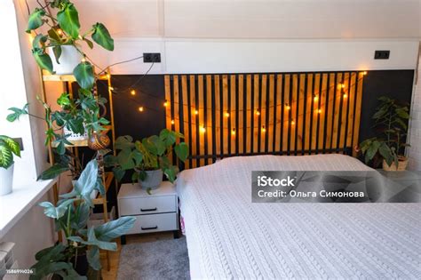 로프트 스타일의 침실 인테리어 나무 칸막이가 있는 검은 벽 금속 침대 복고풍 전구 화환 다락방의 사다리꼴 창문에 화분에 심은 식물 모던 그린 하우스 금속에 대한 스톡 사진