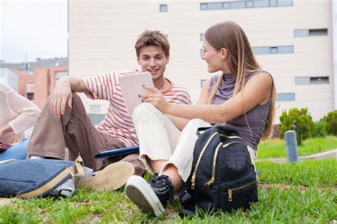 Two College Students Sitting Together On Campus Lawn Reviewing Exam