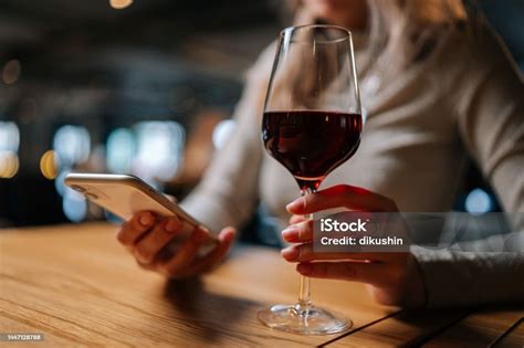 스마트폰을 사용하는 알아볼 수 없는 젊은 여성의 클로즈업 크롭 샷 레스토랑에서 레드 와인 한 잔을 손에 들고 테이블에 앉아 온라인 메시지를 입력합니다 와인에 대한 스톡 사진