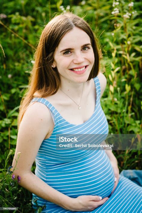 임신 행복 한 여자 앉아서 야외에서 필드에 배경 녹색 잔디에 앉아 위에 손을 잡고 닫습니다 위쪽 절반 카메라를 보고 있습니다 녹색에 대한 스톡 사진 및 기타 이미지 Istock