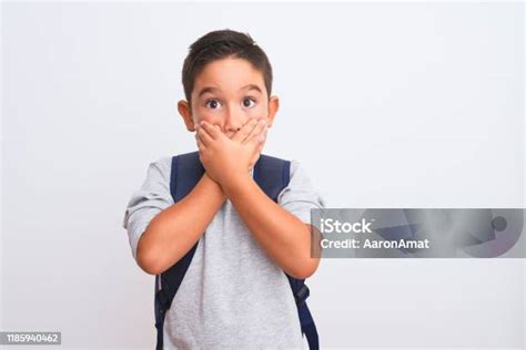 고립 된 흰색 배경 위에 서있는 배낭을 입은 아름다운 학생 아이 소년은 실수로 손으로 입을 덮는 충격을 받았습니다 비밀 개념입니다 가리기에 대한 스톡 사진 및 기타 이미지