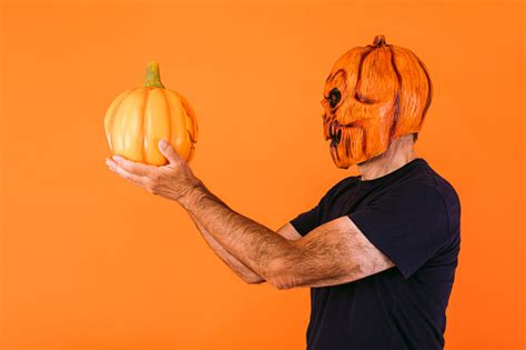 파란 티셔츠를 입은 무서운 호박 라텍스 마스크를 쓰고 있는 남성은 Jacko랜턴 호박을 들고 주황색 배경을 바라보고 있습니다 할로윈과 죽은 개념의 일 10월에 대한 스톡