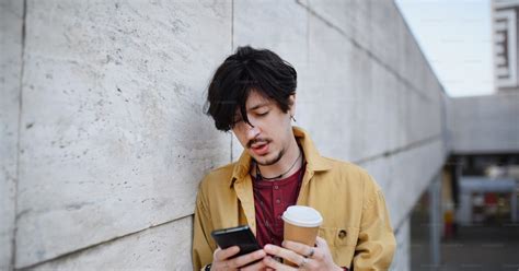 스마트폰을 사용하여 야외에서 콘크리트 벽에 기대어 서 있는 청년의 초상화 사진 Unsplash의 사진술 이미지