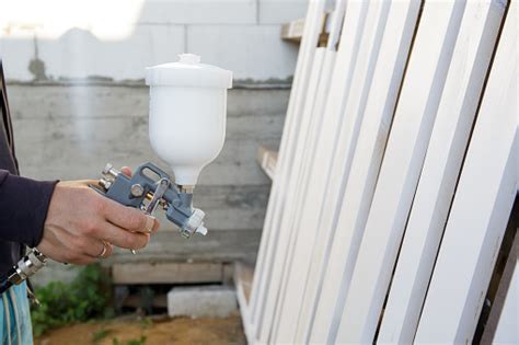 남자의 손에 스프레이 총의 클로즈업 흰색 페인트로 보드를 페인팅하는 과정 마무리 완료 오래된 가구의 복원 압축기 작동 작업 도구