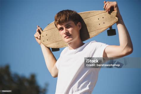스케이트보드를 어깨에 짊어지고 카메라를 바라보며 꿈꾸는 젊은 남자 손에 스케이트 보드와 서 흰색 티셔츠에 젊은 사려 깊은 남자 남자에 대한 스톡 사진 및 기타 이미지