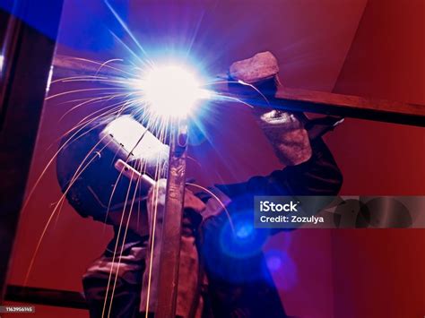 용접기 작업자가 점프 용접을 수행합니다 작업자 용접기는 금속 구조물의 아크 용접 공정을 수행합니다 용접 기계에서 불꽃 비행 용접기 용접 금속 프로파일 2 층 실내 강철에