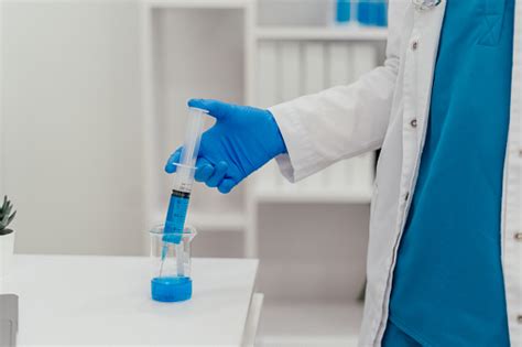 파란 장갑을 낀 의사가 실험실 비커 위에 파란 액체가 든 주사기를 들고 있다 이 이미지는 의료 정밀도 실험실 작업 및 의료
