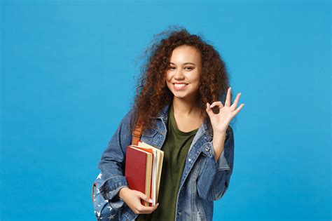 데님 옷에 젊은 아프리카계 미국인 소녀 사춘기 학생 배낭은 파란색 벽 배경 스튜디오 초상화에 고립 된 책을 잡아 고등학교 대학 대학 개념에서 교육 복사 공간을 모의 가방에