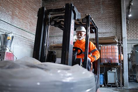 공장 보관실에서 지게차 기계를 작동하는 유니폼과 흰색 하드 햇을 사용하는 수석 백인 남성 Brand Name Video Game에 대한 스톡 사진 및 기타 이미지