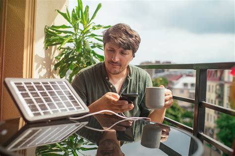 화창한 여름날 발코니에서 태양 전지판으로 스마트폰을 충전하는 남자 지속 가능한 라이프 스타일 태양 에너지 생태 대체 에너지 및 생태 개념 발코니에 대한 스톡 사진 및 기타