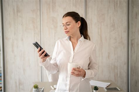 휴대 전화를 사용하여 직장에서 사무실에 서있는 한 여성 사업가 25 29세에 대한 스톡 사진 및 기타 이미지 25 29세 Brand Name Smart Phone