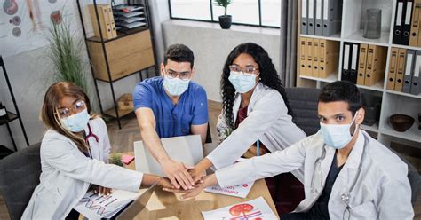 성공 팀워크 개념 마스크를 쓴 다인종 과학자 팀이 현대 병원의 테이블에 앉아 손을 모으고 있다 국제 협력 및 건강 관리의 개념 사진 Unsplash의 작업 이미지