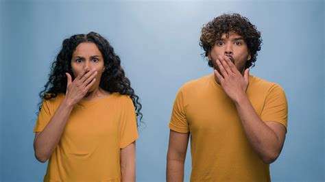 다인종 충격 무서움 커플 놀람 히스패닉 여자 뒤에 숨어있는 인도 남자 놀라움 경이로움 무서운 공포 추악한 반응 파란색 스튜디오 배경 충격 놀람 공포 공포 2명에 대한 스톡