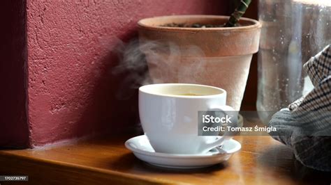 맛있는 뜨거운 커피 또는 따뜻한 차로 가득 찬 하얀 컵이 창문 근처의 테이블에 누워 물건 클로즈업 측면보기 세부 사항 증기 위 휴식 레저 모닝 커피 추상적 인 개념 아무도