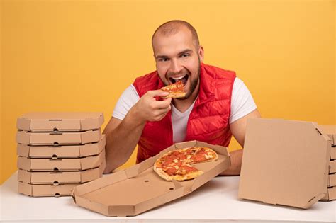 테이블에 앉아 젊은 잘 생긴 사람 피자 상자의 큰 숫자 주위에 노란색 배경 위에 피자를 먹고 가리키기에 대한 스톡 사진 및 기타