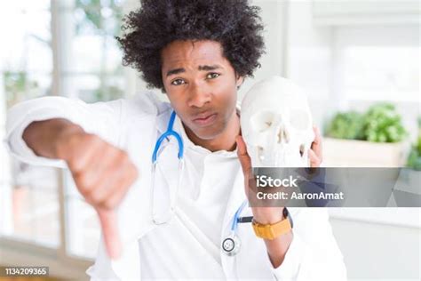 아프리카계 미국인 닥터 남자는 화난 얼굴로 두개골을 들고 아래로 엄지 손가락으로 혐오를 보여주는 부정적인 기호 거절 개념 개념에 대한 스톡 사진 및 기타 이미지 Istock