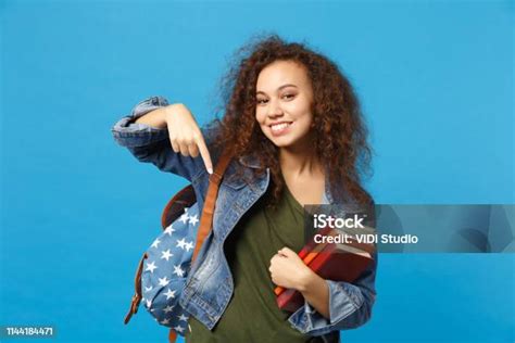 데님 옷에 젊은 아프리카계 미국인 소녀 사춘기 학생 배낭은 파란색 벽 배경 스튜디오 초상화에 고립 된 책을 잡아 고등학교 대학 대학 개념에서 교육 복사 공간을 모의 가방에