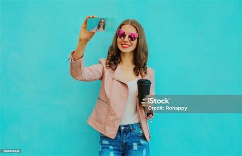 파란 배경에 커피 한 잔과 함께 스마트 폰으로 셀카를 찍는 미소 짓는 젊은 여성의 초상화 셀카에 대한 스톡 사진 및 기타 이미지