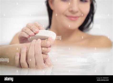 Woman Relaxing In A Hot Soapy Bath Using A Pumice Stone To Exfoliate Her Feet And Remove Dead