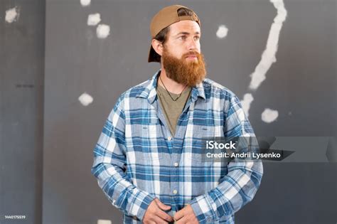 셔츠를 입고 벽을 배경으로 야구 모자를 쓴 수염 난 남자 수리 및 개조 주택 30 34세에 대한 스톡 사진 및 기타 이미지 30 34세 개선 건물 외관 Istock