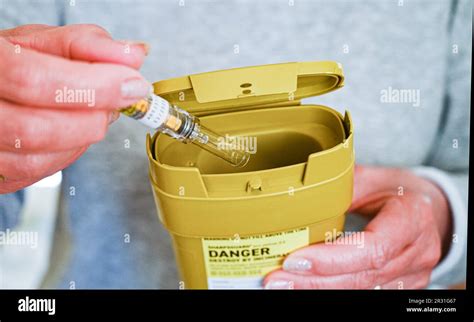 Woman Disposing Of A Used Needle In A Sharpsguard Disposal Waste Unit Or Sharps Bin Stock Photo