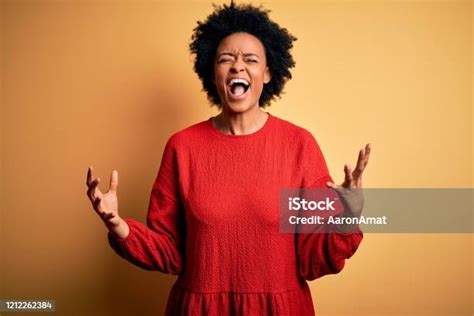 젊은 아름 다운 아프리카 계 미국인 Afro 여자 곱슬 머리 캐주얼 스웨터를 입고 미친 미친 소리와 공격적인 표정과 팔을 제기 고함 좌절 개념입니다 감정에 대한 스톡 사진