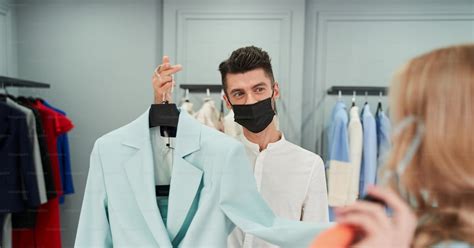 새로운 구매가 있습니다 보호 마스크를 착용한 조수와 함께 쇼룸에 서 있는 동안 선반에서 옷을 고르는 사려 깊은 젊은 여성 사진 Unsplash의 소매점 이미지