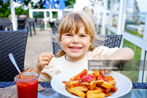 야외 테라스에 레스토랑에서 토마토 케첩과 감자 튀김을 먹는 행복 미소 유치원 소녀의 초상화 금발 머리를 가진 어린 아이는 건강에 해로운 패스트 푸드 또는 신선한 준비 점심을