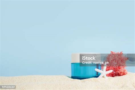 파란색 유리병에 담긴 화장품 크림은 불가사리와 파란색 배경의 모래 위에 분홍색 해초가 있고 공간을 복사합니다 Uva 및 Uvb 보호 여름 화장품 모래에 대한 스톡 사진 및