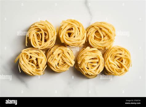 Dry Tagliolini Or Tagliatelle Pasta In Nests In The Bowl On White Marble Background Uncooked