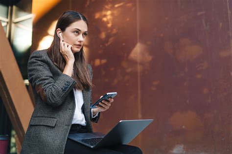 노트북을 사용하여 사무실 건물 앞 계단 위에 앉아 전화기를 들고 있는 젊은 여성의 초상화 야외에서 개인용 컴퓨터를 사용하는 사람 매력적인 아름다운 소녀 25 29세에 대한