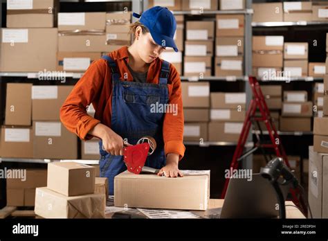 Female Worker Packing Cardboard Box With Tape Gun Dispenser In Warehouse Woman Employee Packing