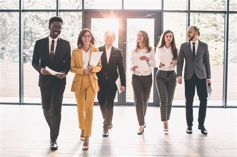 카메라를 향해 걷는 비즈니스 사람들 큰 창이 있는 현대 사무실에서 일 회의를 갖는 정장 복장의 행복한 젊은 사업가의 전체 길이 경영자에 대한 스톡 사진 및 기타 이미지