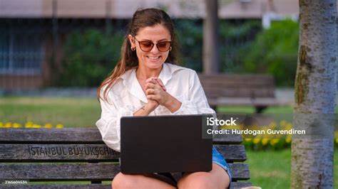 공원 벤치에 앉아 무릎 위에 올려놓고 노트북으로 작업하는 아름다운 중년 사업가가 성공에 대한 기쁨과 흥분을 명확하게 전달하는 몸짓과 표정을 보여주고 있습니다 35 39세에